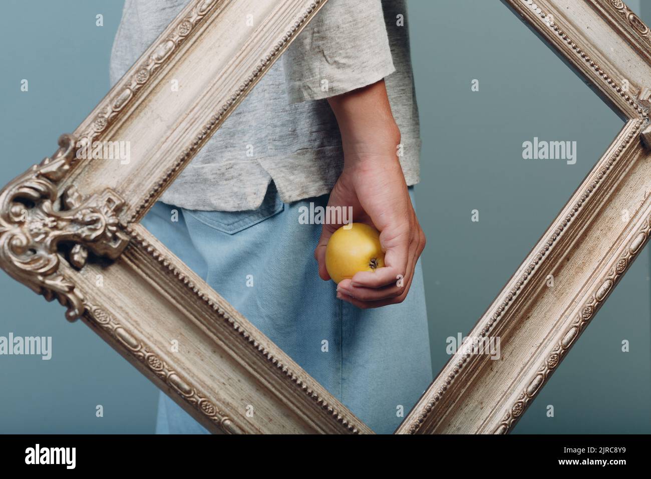 Millenial young man holds apple on hand palm in gilded picture frame ...