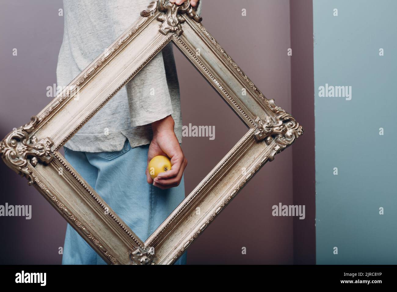 Millenial young man holds apple on hand palm in gilded picture frame ...