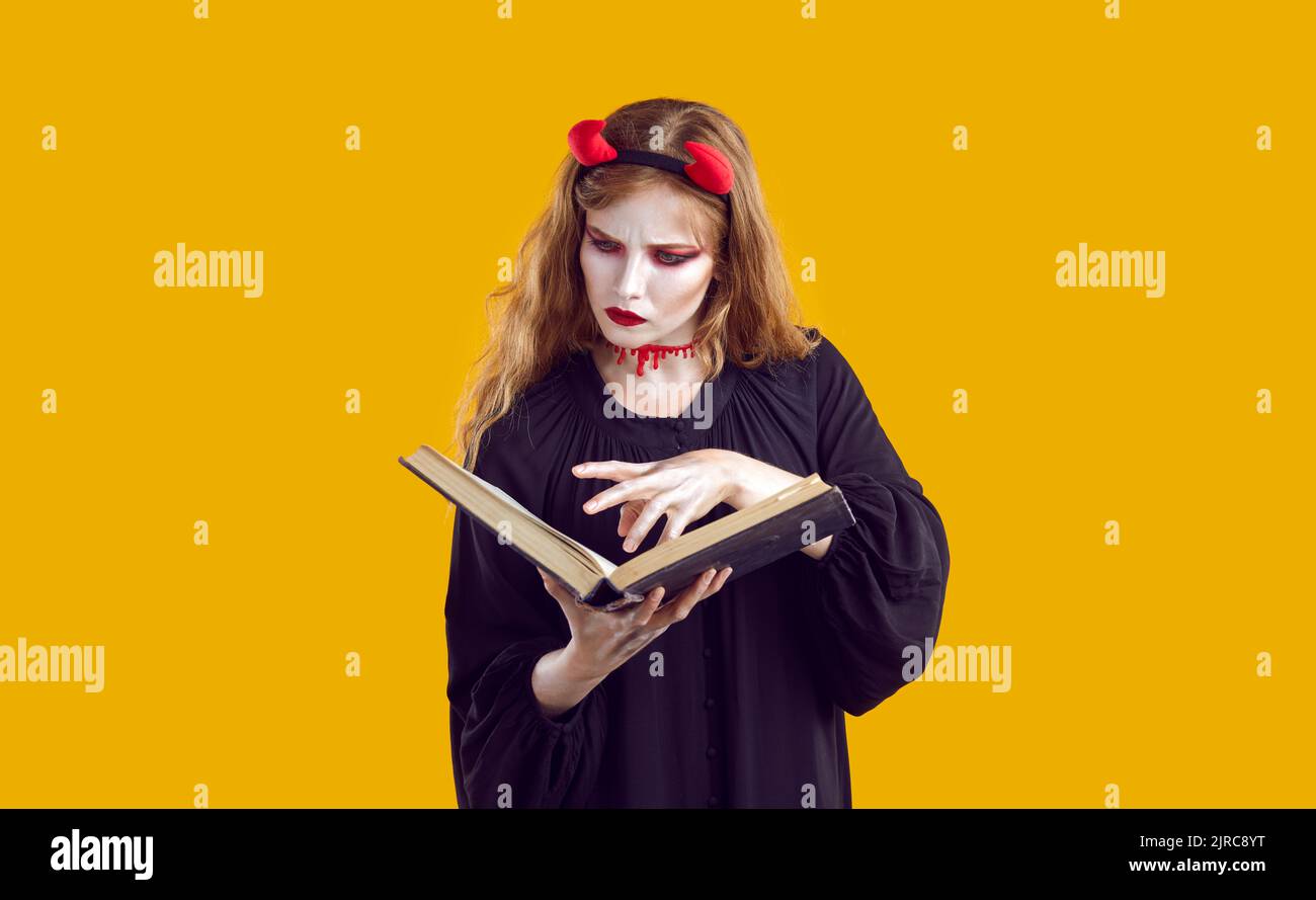 Young woman dressed in scary Halloween costume reading book of evil ...