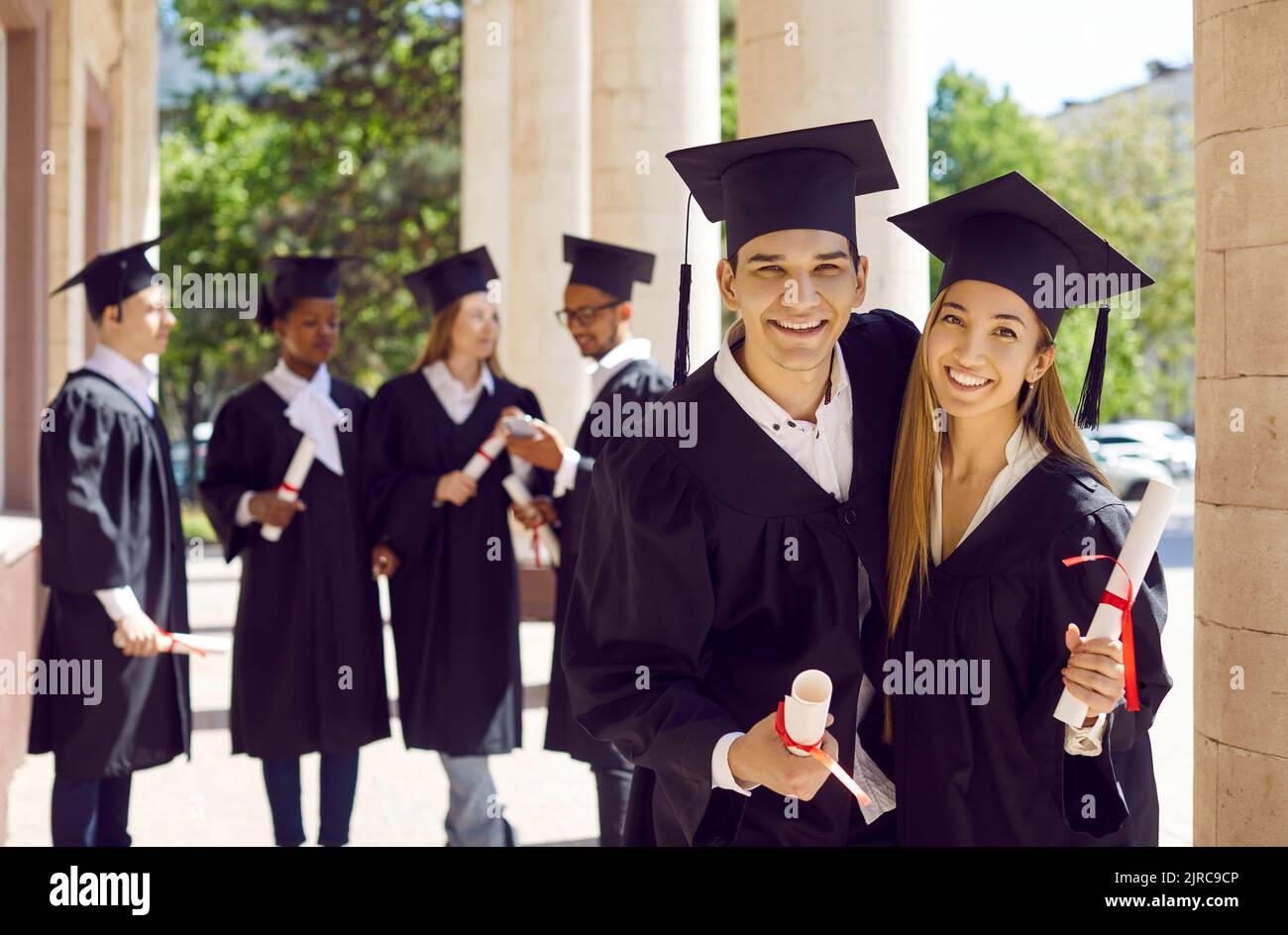 Portrait of happy friends with diplomas hugging and smiling on their ...