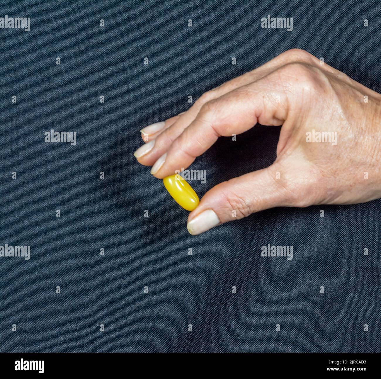 A yellow pill held by the fingers of one hand against a black ...