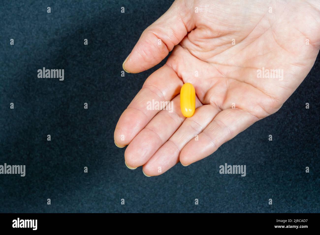 A yellow pill in the palm of a hand against a black background. Medical ...