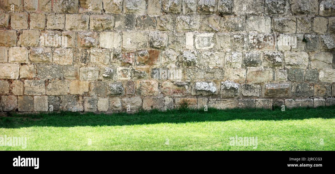 Background with an ancient wall and green grass lit by the sun Stock ...