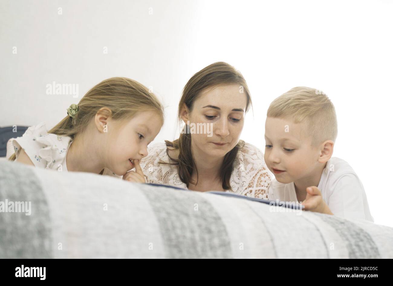 Children lie on the bed in the bedroom, mother reads a book to them ...