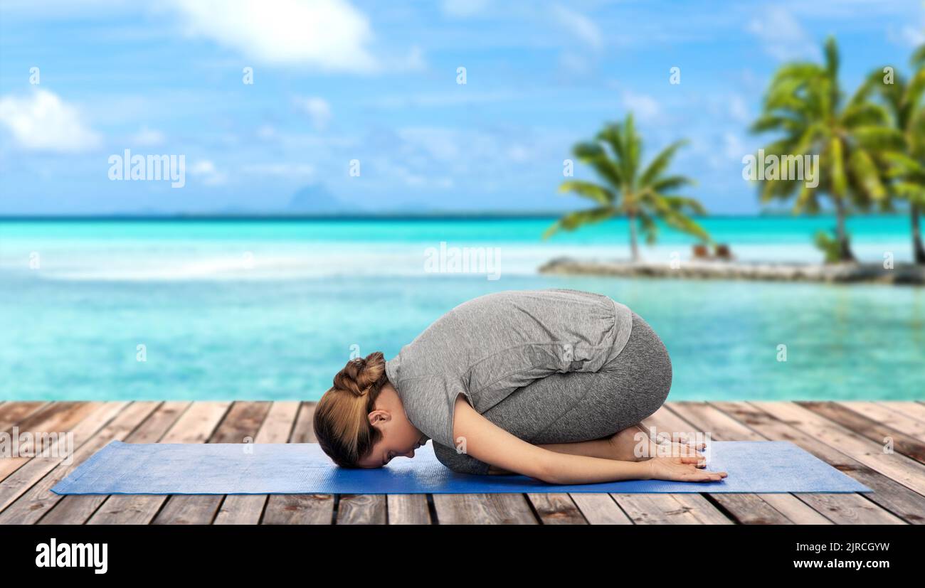 woman doing yoga child pose on mat over ocean Stock Photo - Alamy