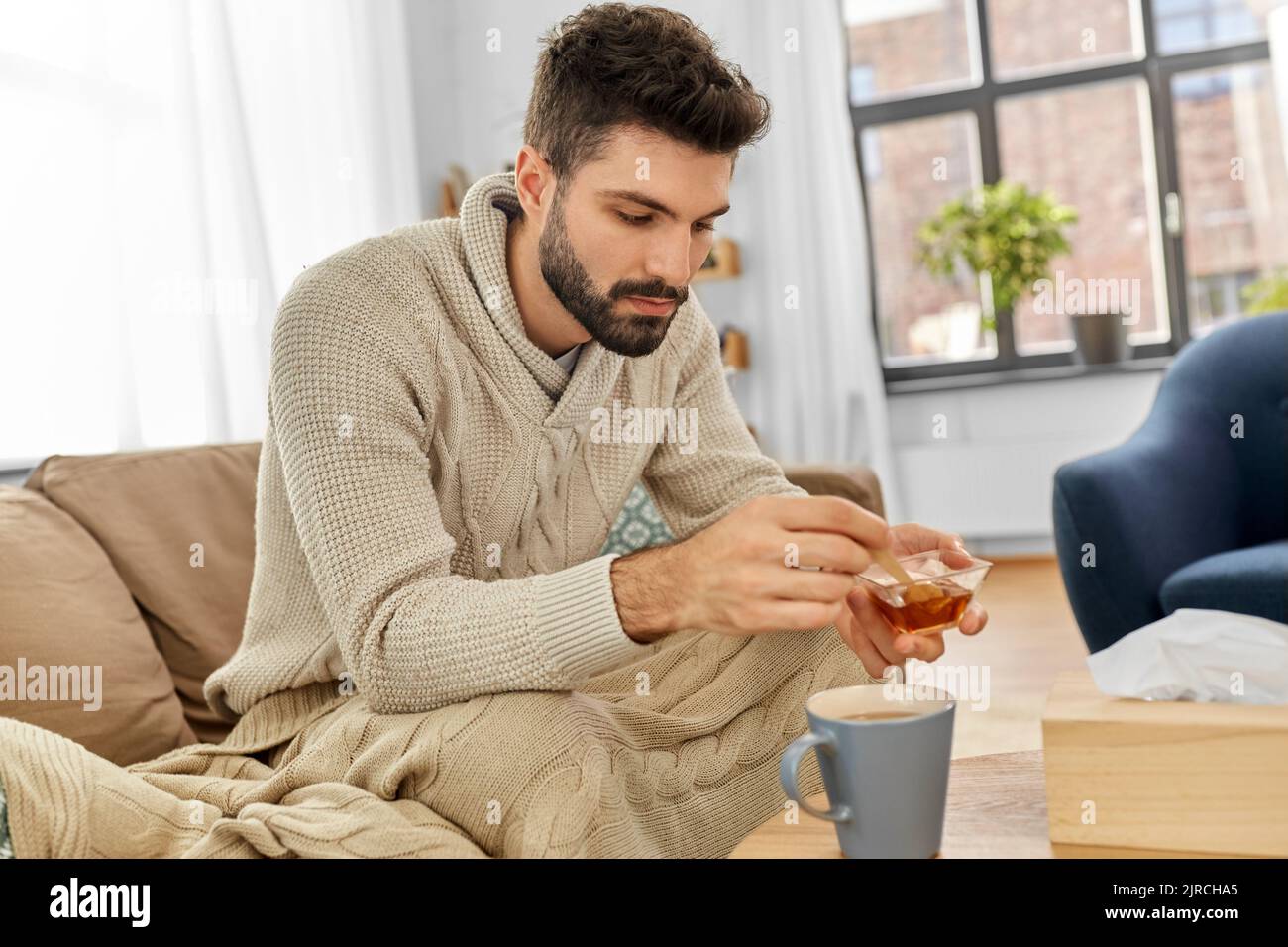 sick young man in blanket drinking hot tea at home Stock Photo - Alamy