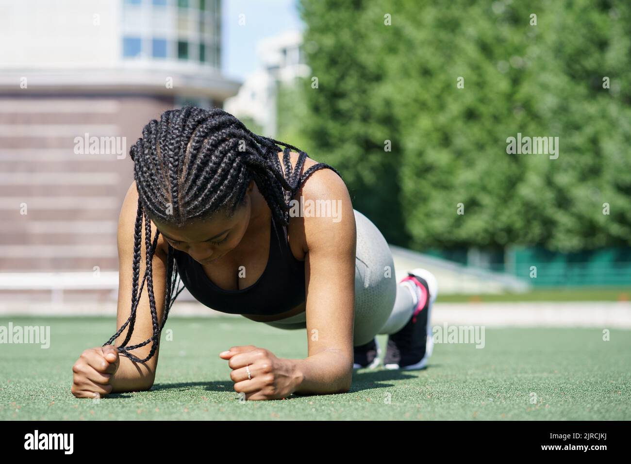 African American woman with long braids does plank exercise on green ...