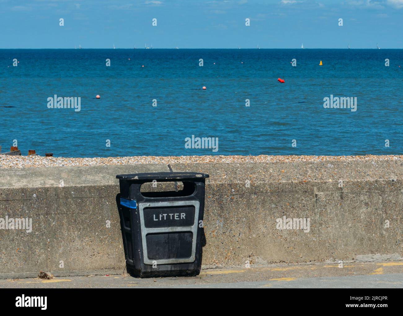 A black litter bin against concrete fence on the lakeshore in Whistable ...