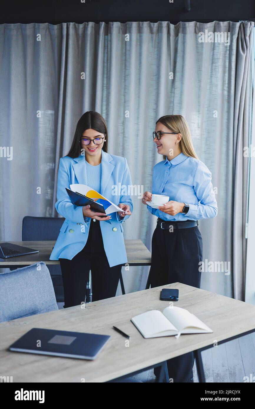 Two young women managers work in a modern office. Women colleagues are talking while working ...