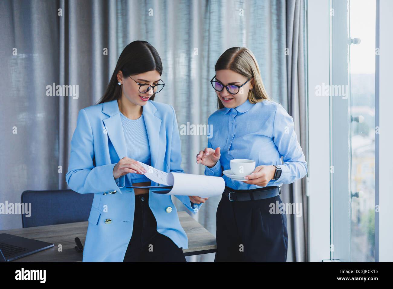 Two young women managers work in a modern office. Women colleagues are ...