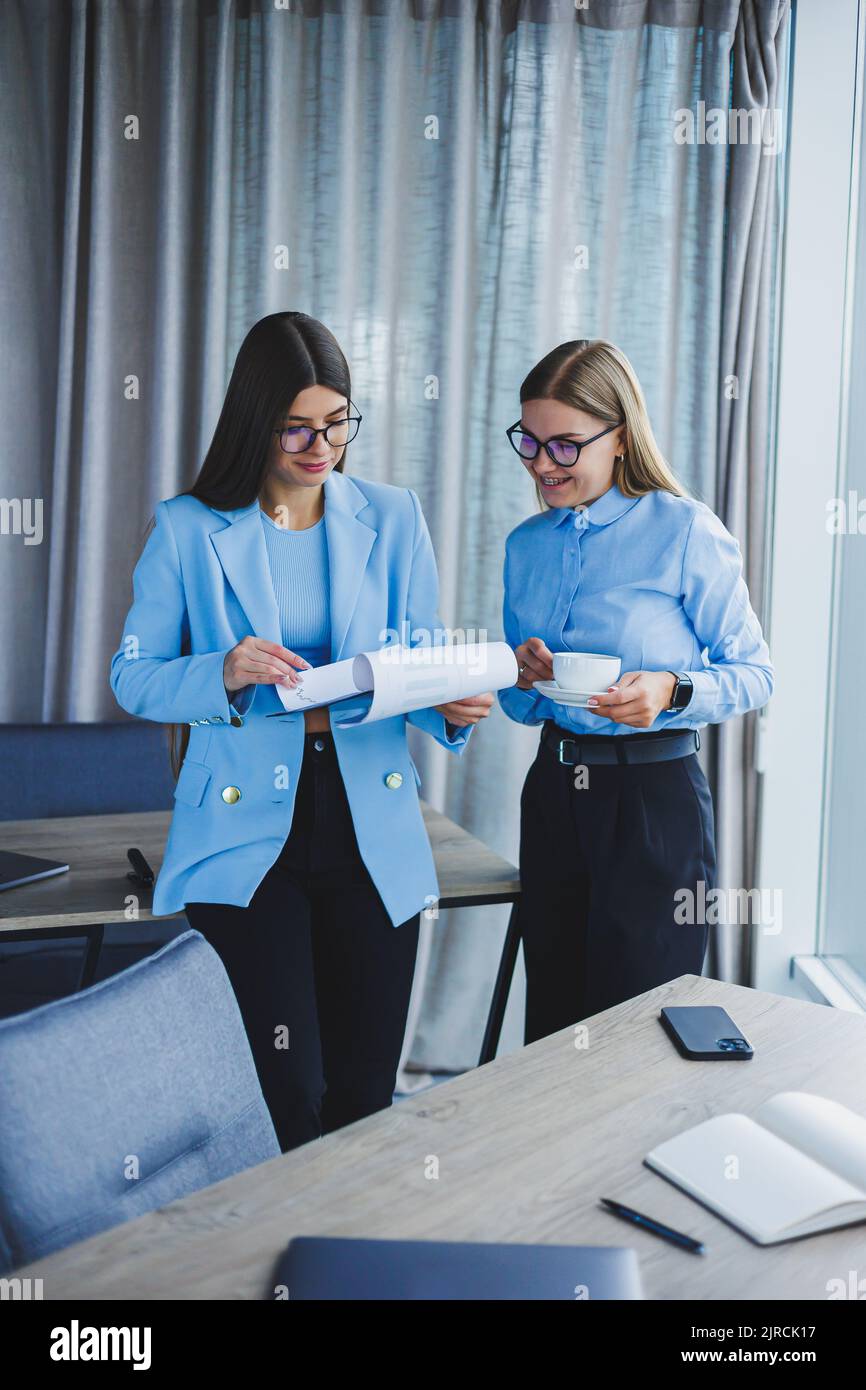 Two young women managers work in a modern office. Women colleagues are talking while working ...