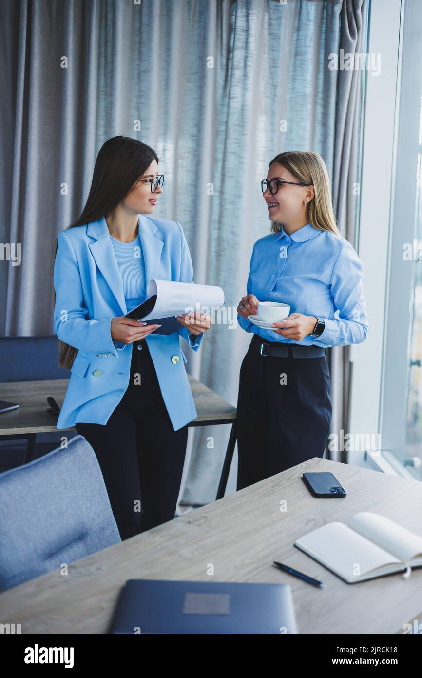 Two young women managers work in a modern office. Women colleagues are ...