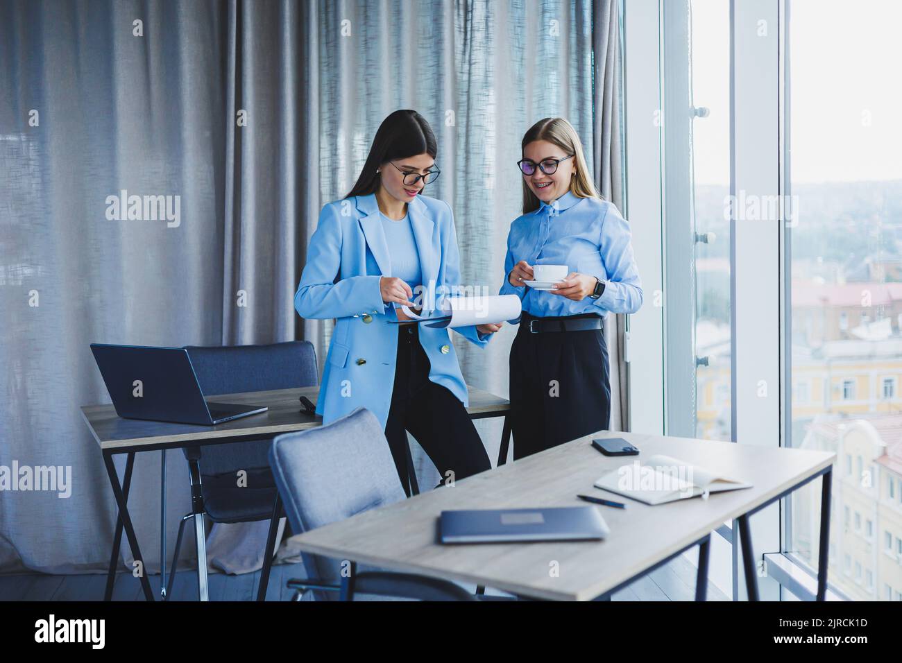 Two young women managers work in a modern office. Women colleagues are talking while working ...