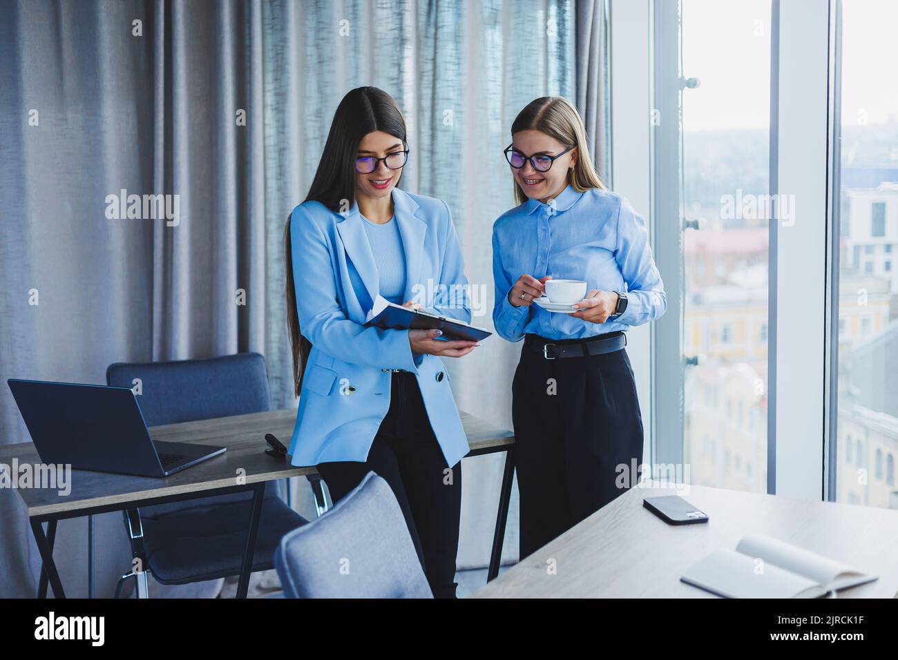 Two young women managers work in a modern office. Women colleagues are ...