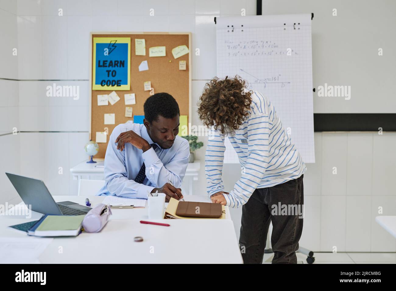 Portrait of young black teacher helping boy with task or grading ...
