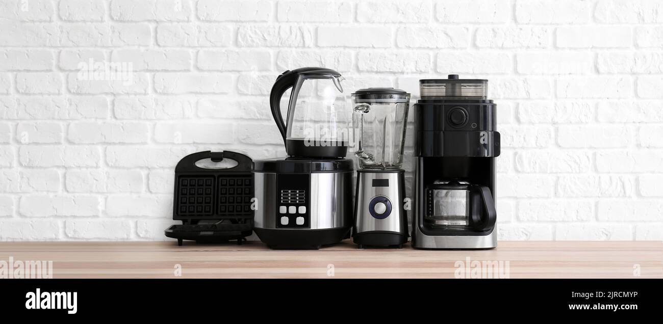 Different household appliances on table against white brick background ...