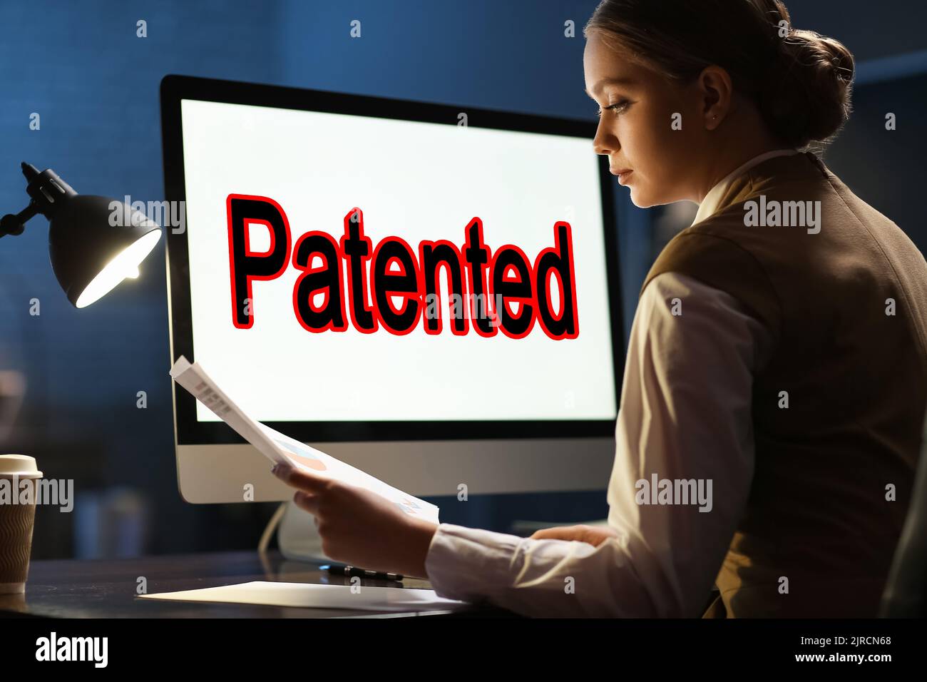 Young woman sitting near computer monitor with word PATENTED in office ...