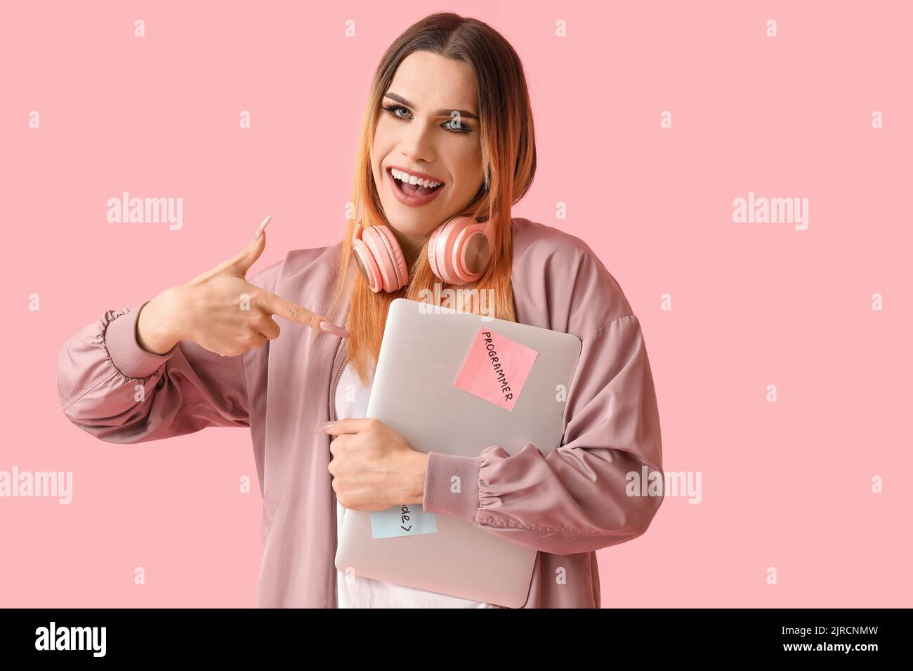 Transgender programmer with laptop and headphones on pink background ...