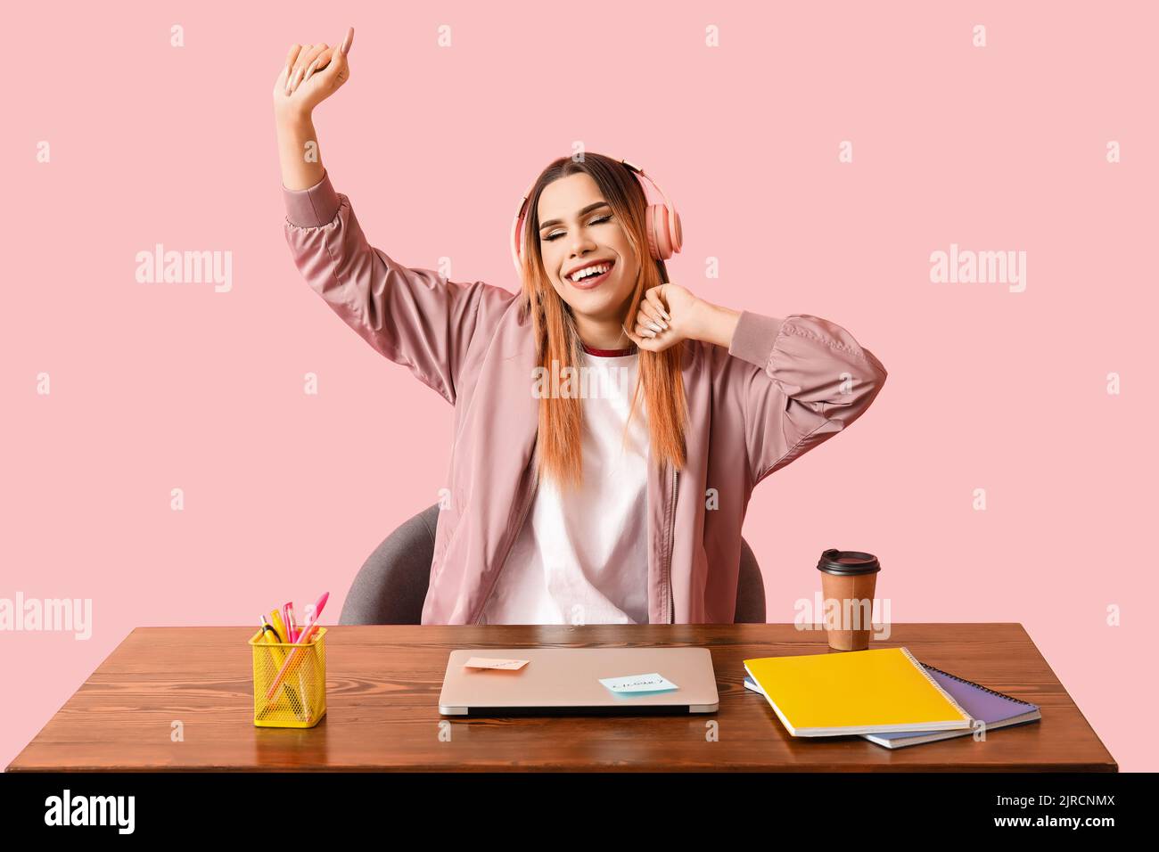 Transgender programmer with laptop at table on pink background Stock ...