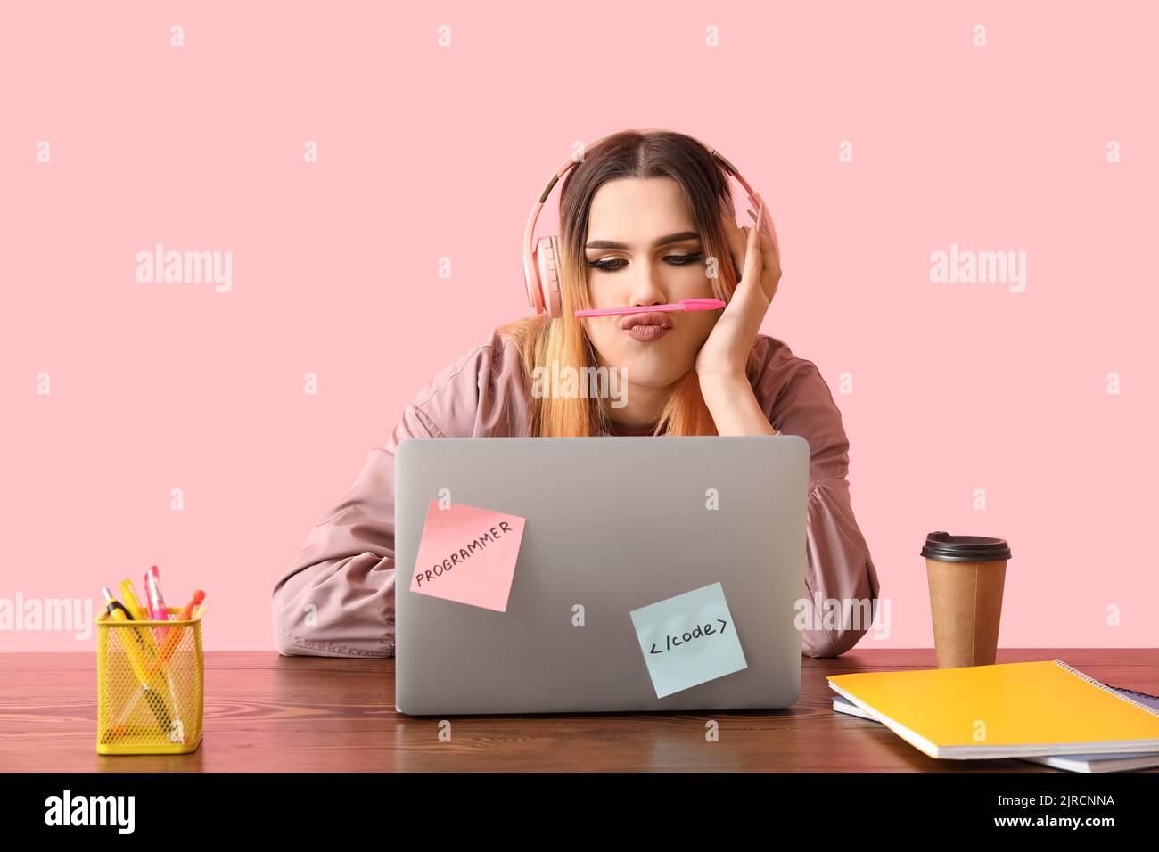 Funny transgender programmer with laptop at table on pink background ...
