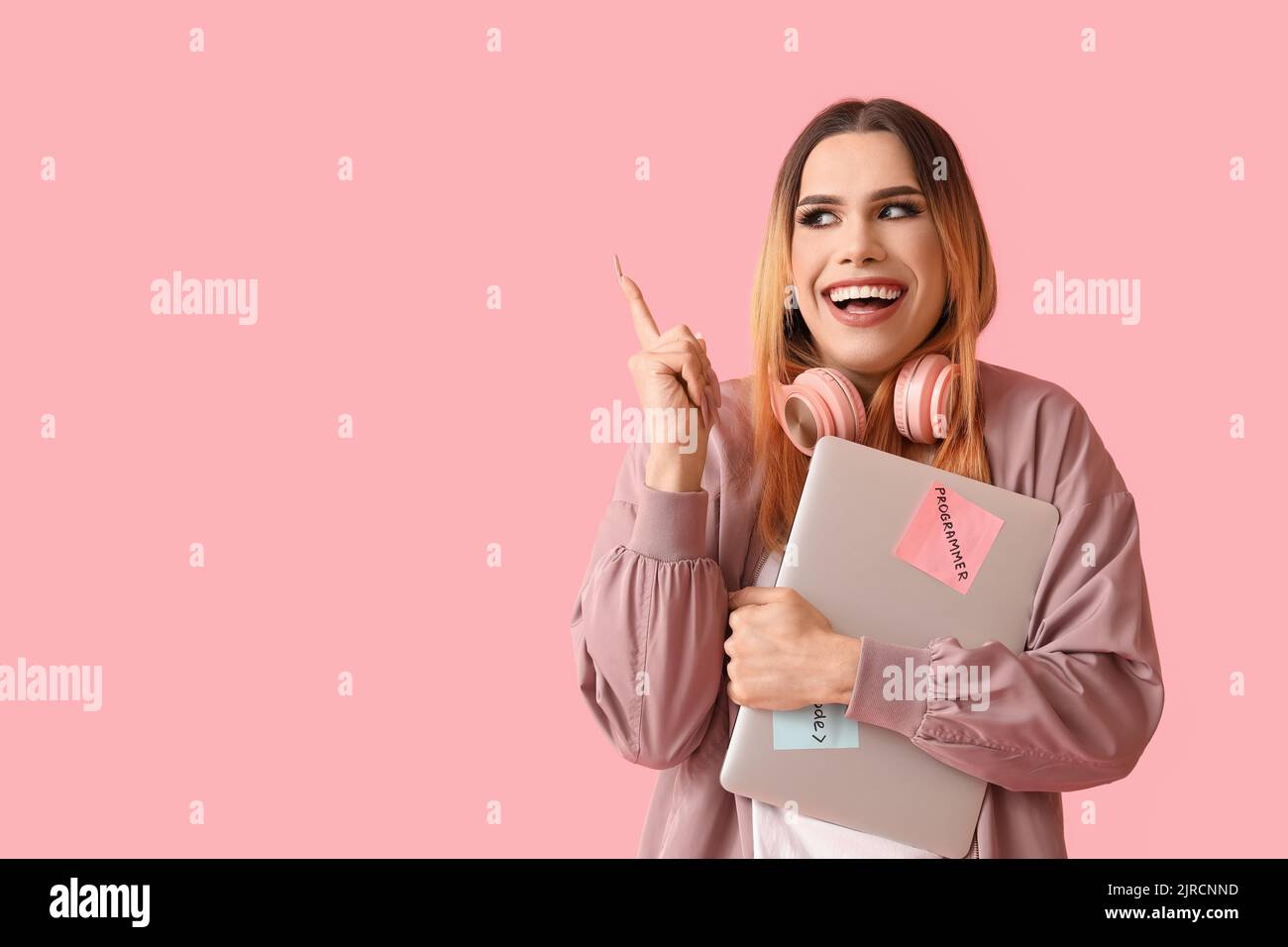 Transgender programmer with laptop pointing at something on pink ...