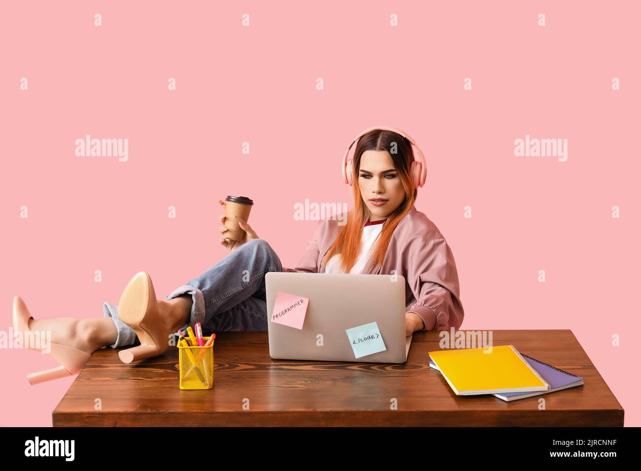 Transgender programmer with laptop at table on pink background Stock ...