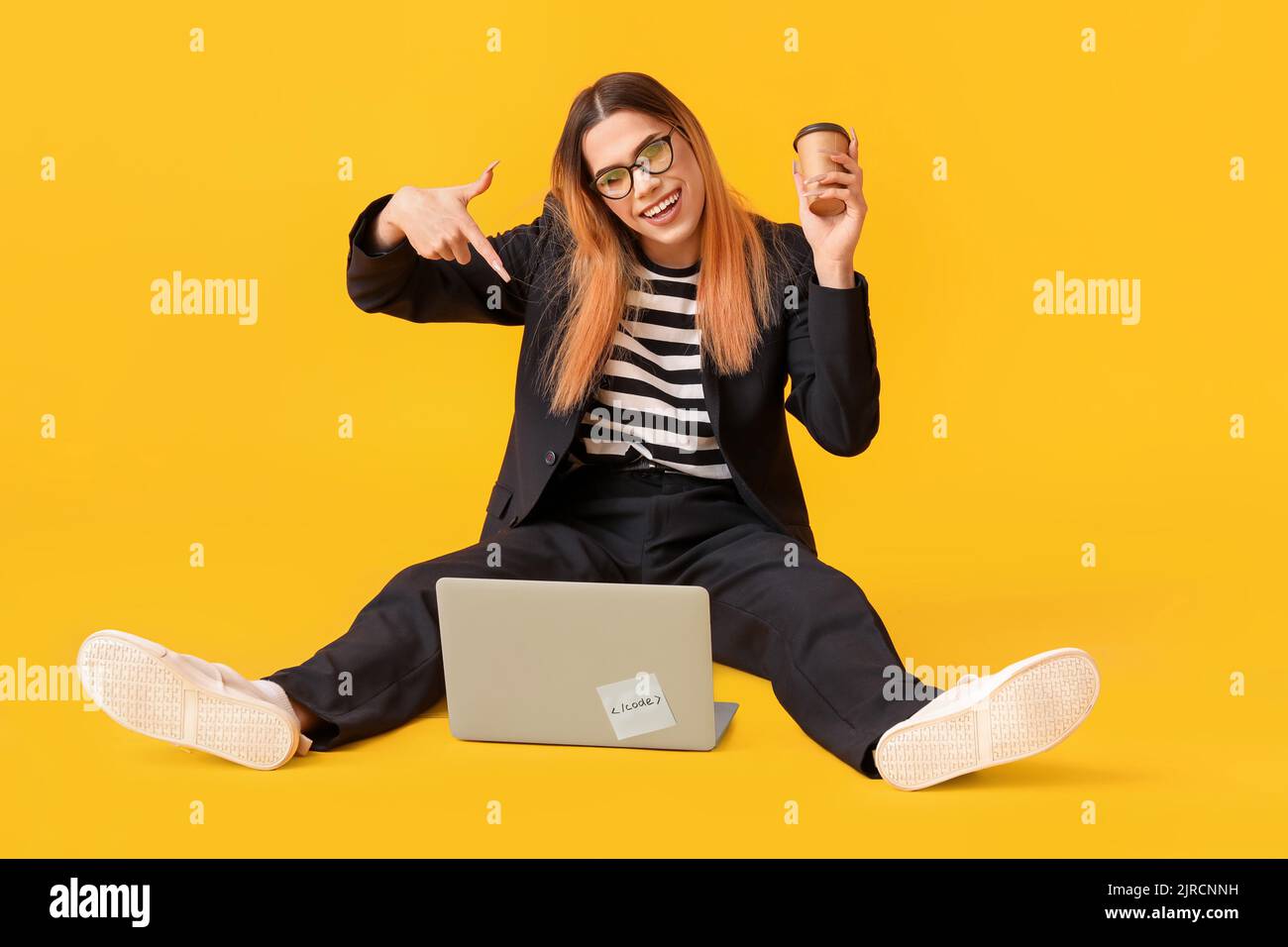 Transgender programmer with laptop and coffee on yellow background ...