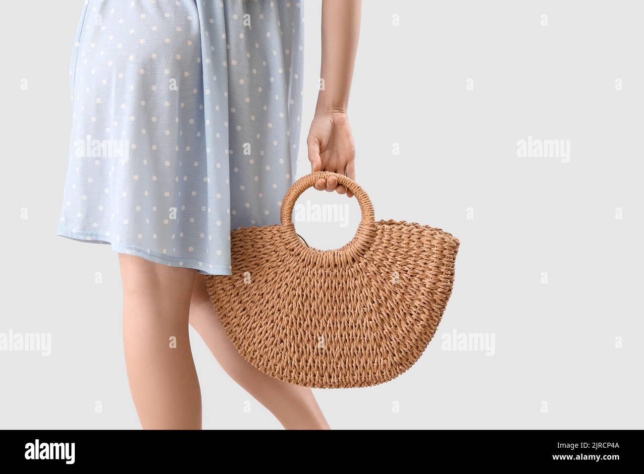Young woman holding rattan bag behind her back on light background ...