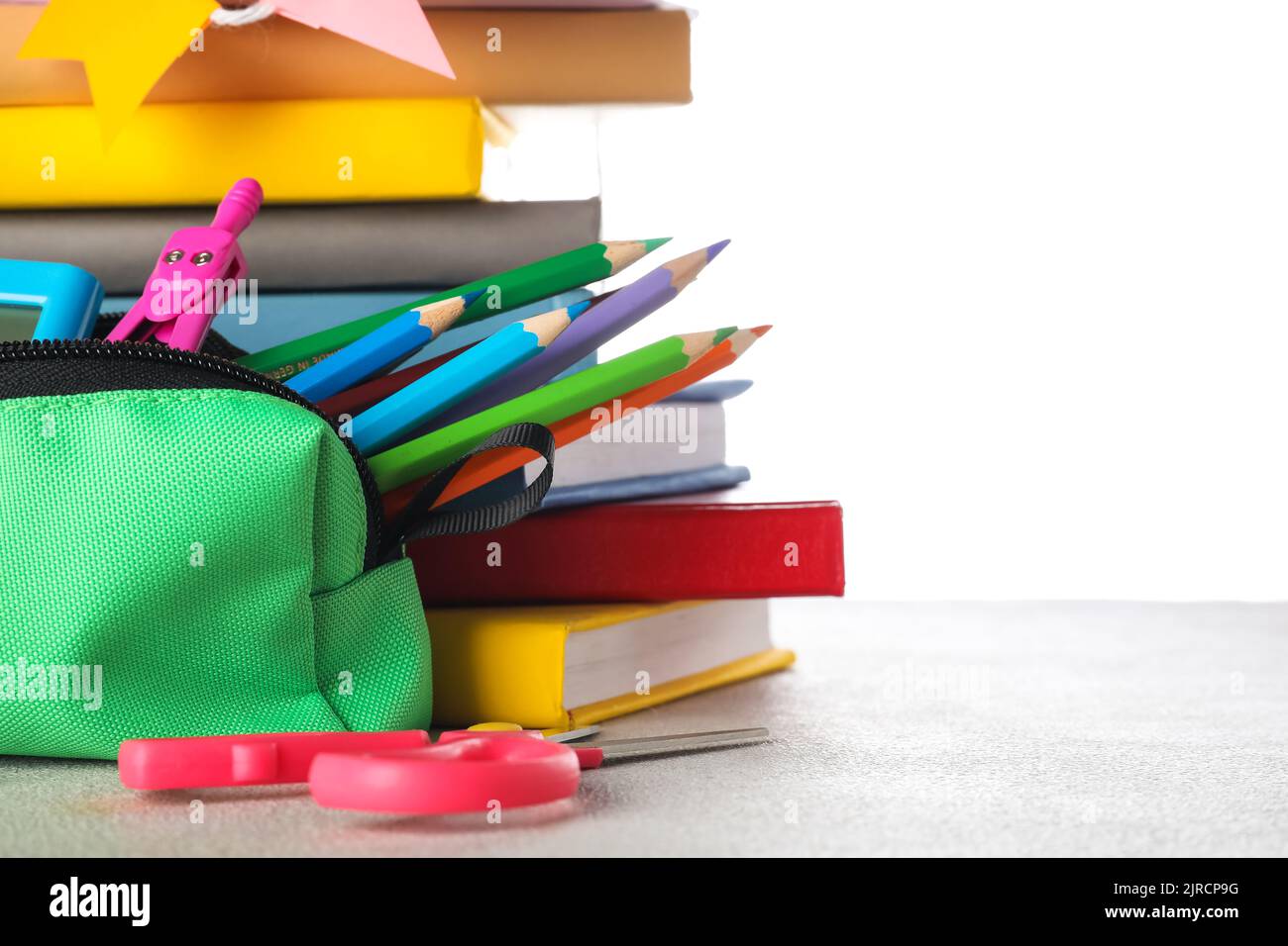 Green pencil case with school stationery and books on table against ...