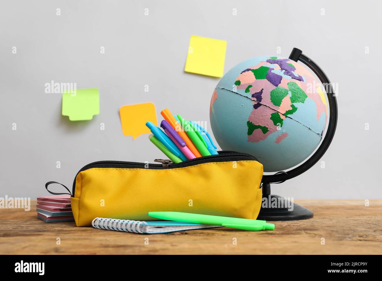Yellow pencil case with school stationery and globe on table against ...