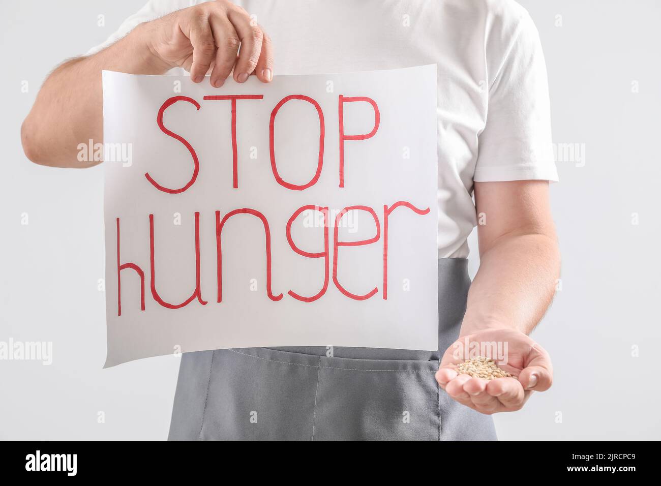 Man holding paper sheet with text STOP HUNGER and wheat grains on light ...