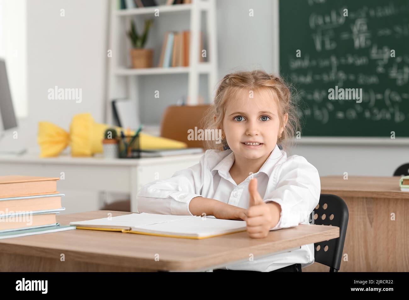 Cute little first-grader showing thumb-up at desk in classroom Stock ...