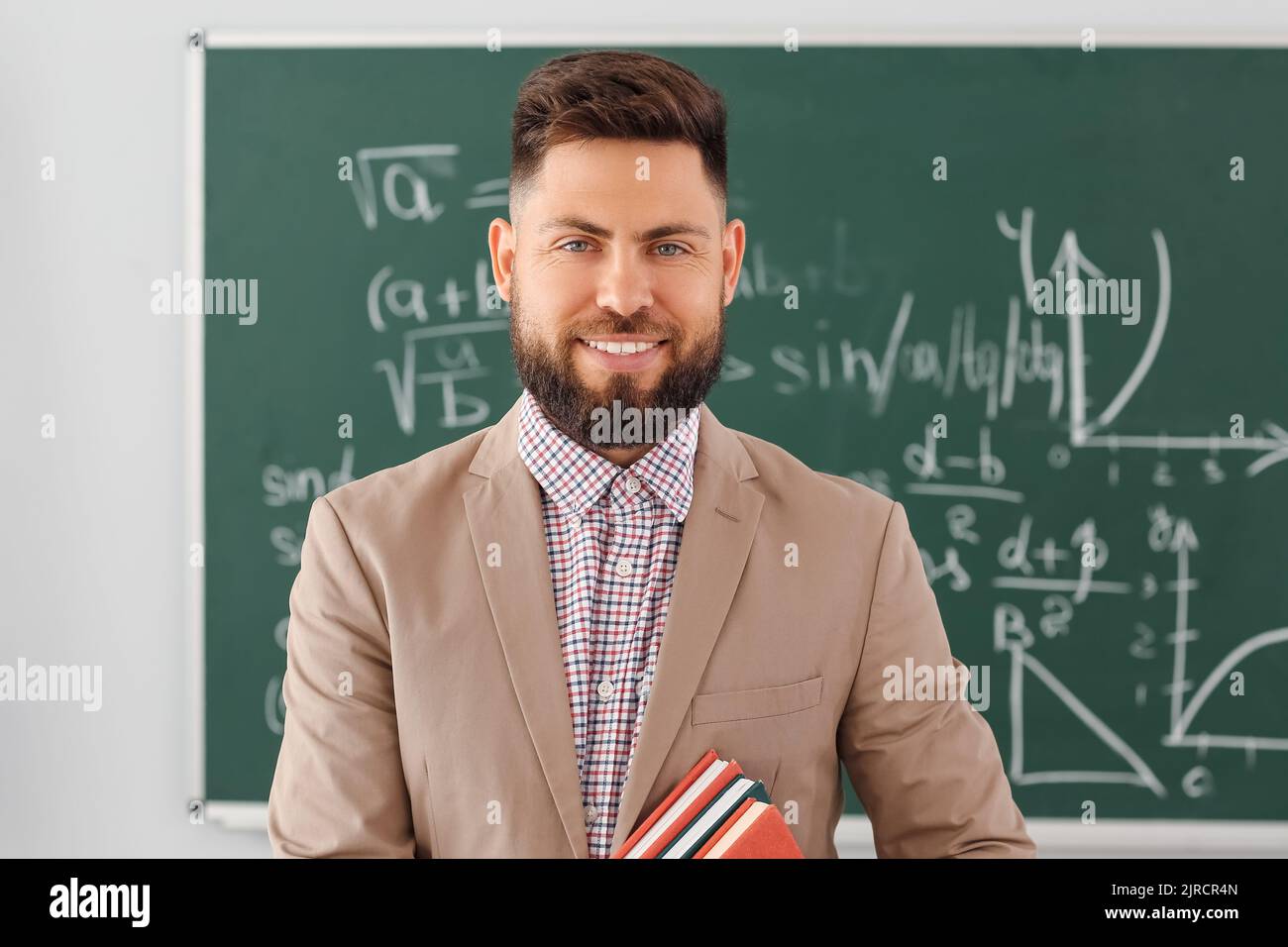 Handsome Math teacher with books in classroom Stock Photo - Alamy