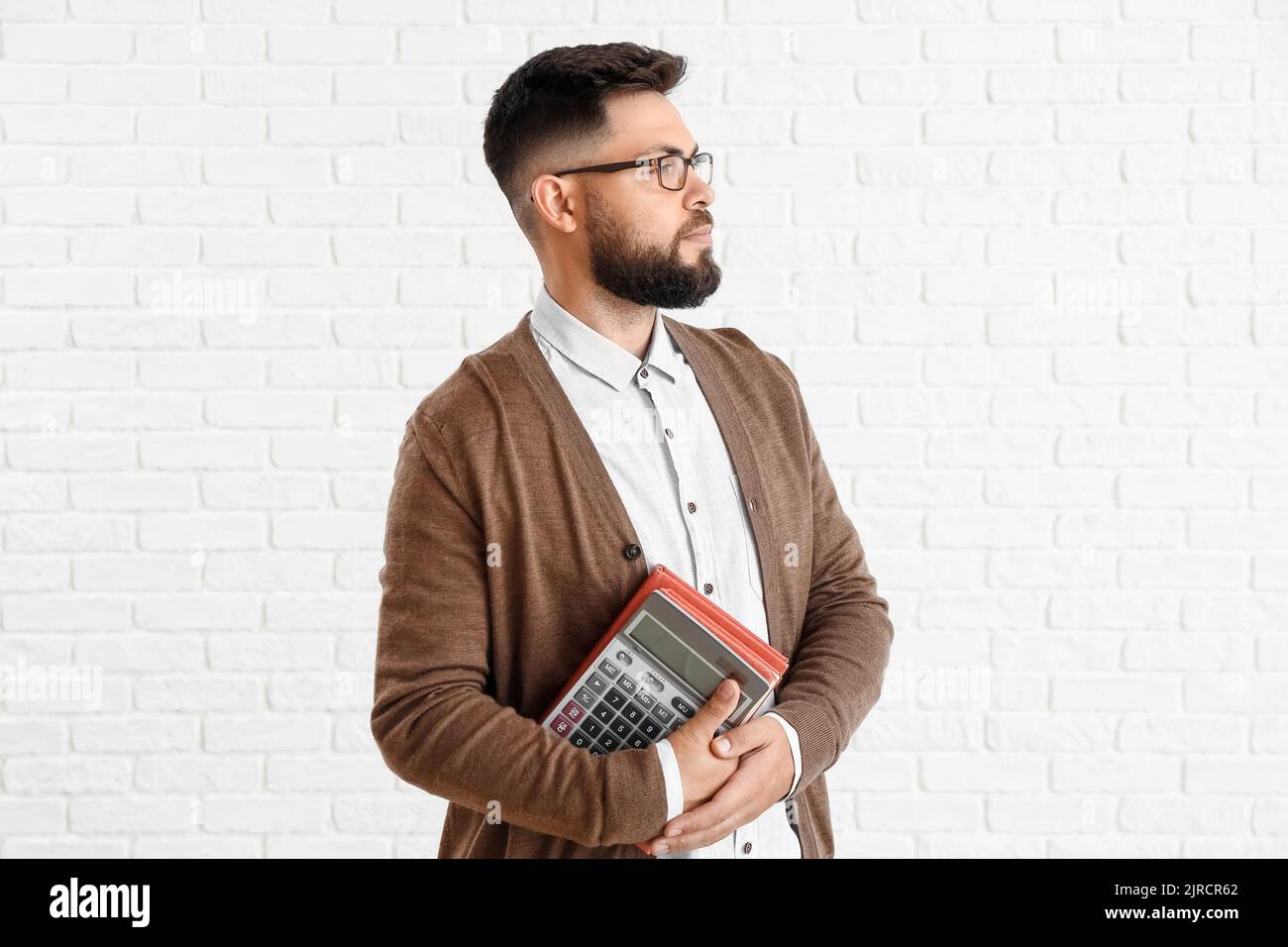 Handsome Math teacher with calculator and books on white brick ...