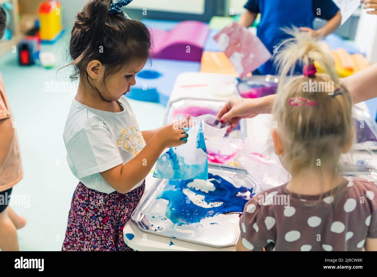 Multicultural group of children milk painting with the teacher helping ...