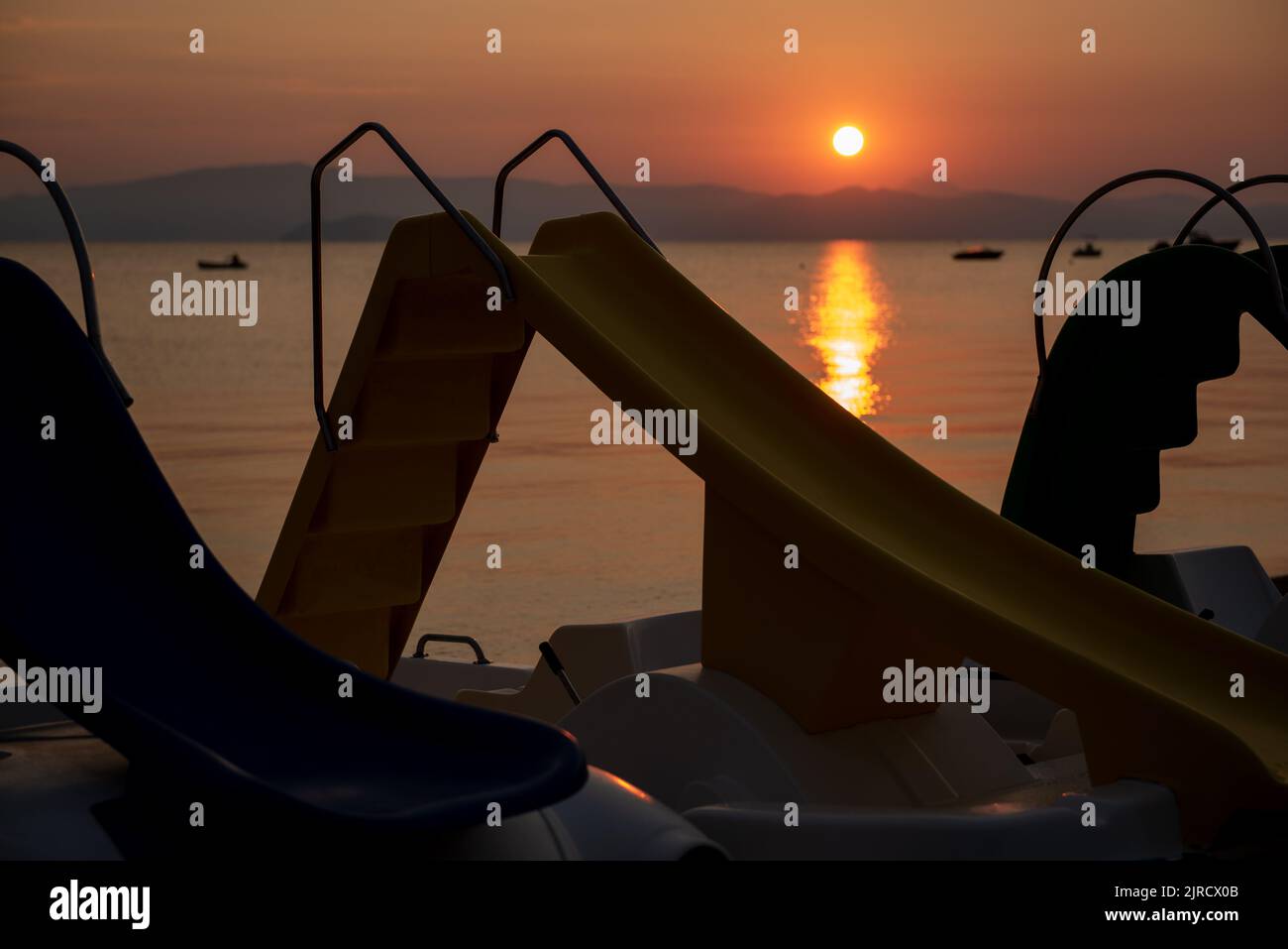 Water slides and pedalos sat on beach with sunrise/sunset in the ...
