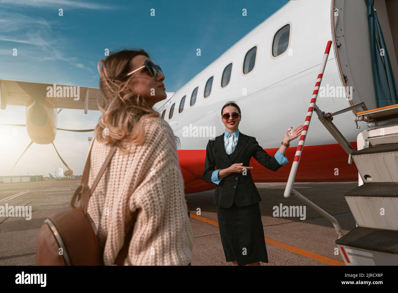 Woman stewardess standing near airplane and inviting female passenger ...