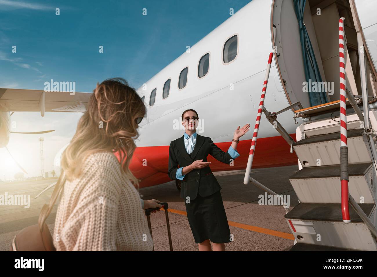 Woman stewardess standing near airplane and inviting female passenger ...