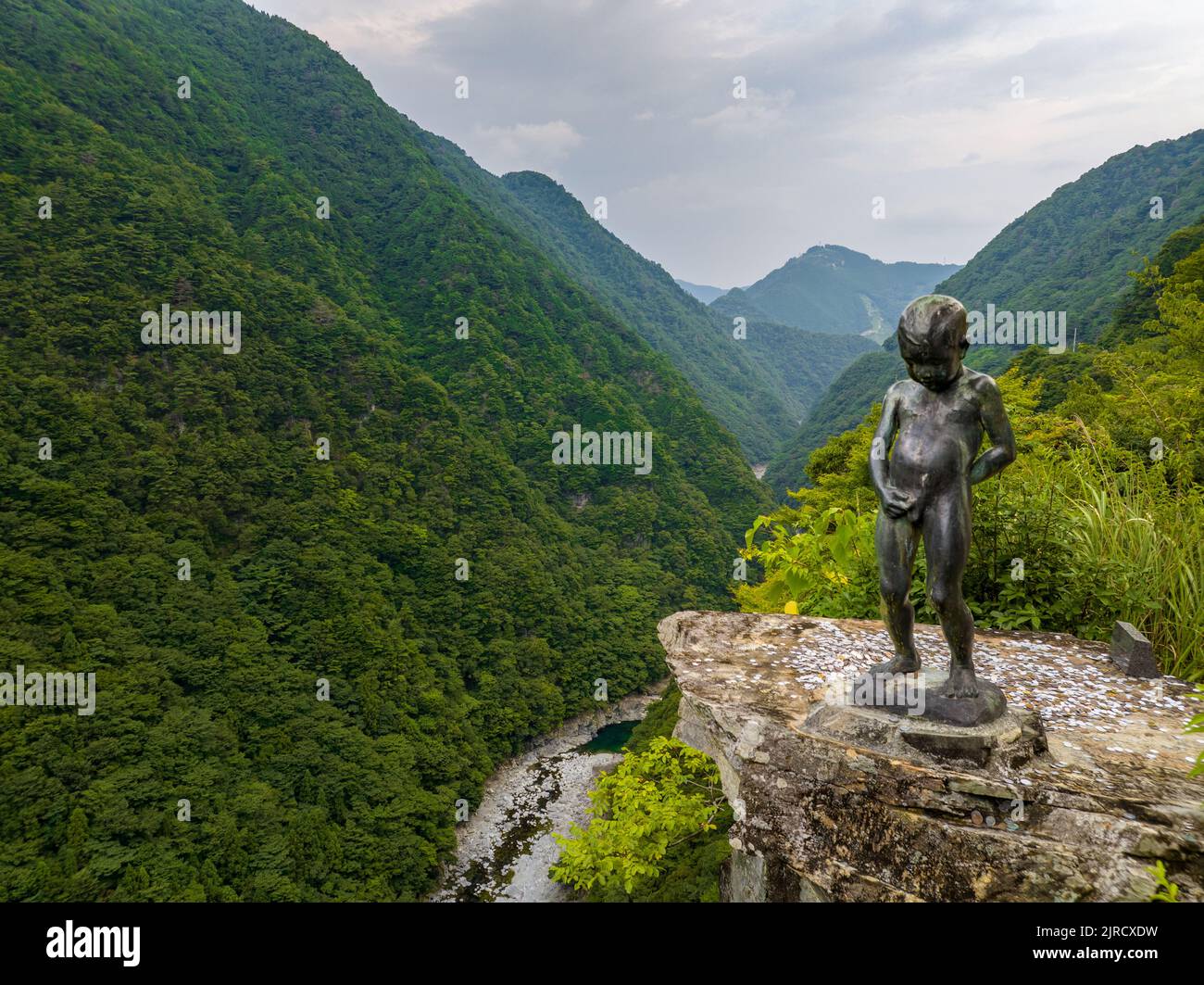 Statue of boy peeing into deep canyon river in forested valley ...