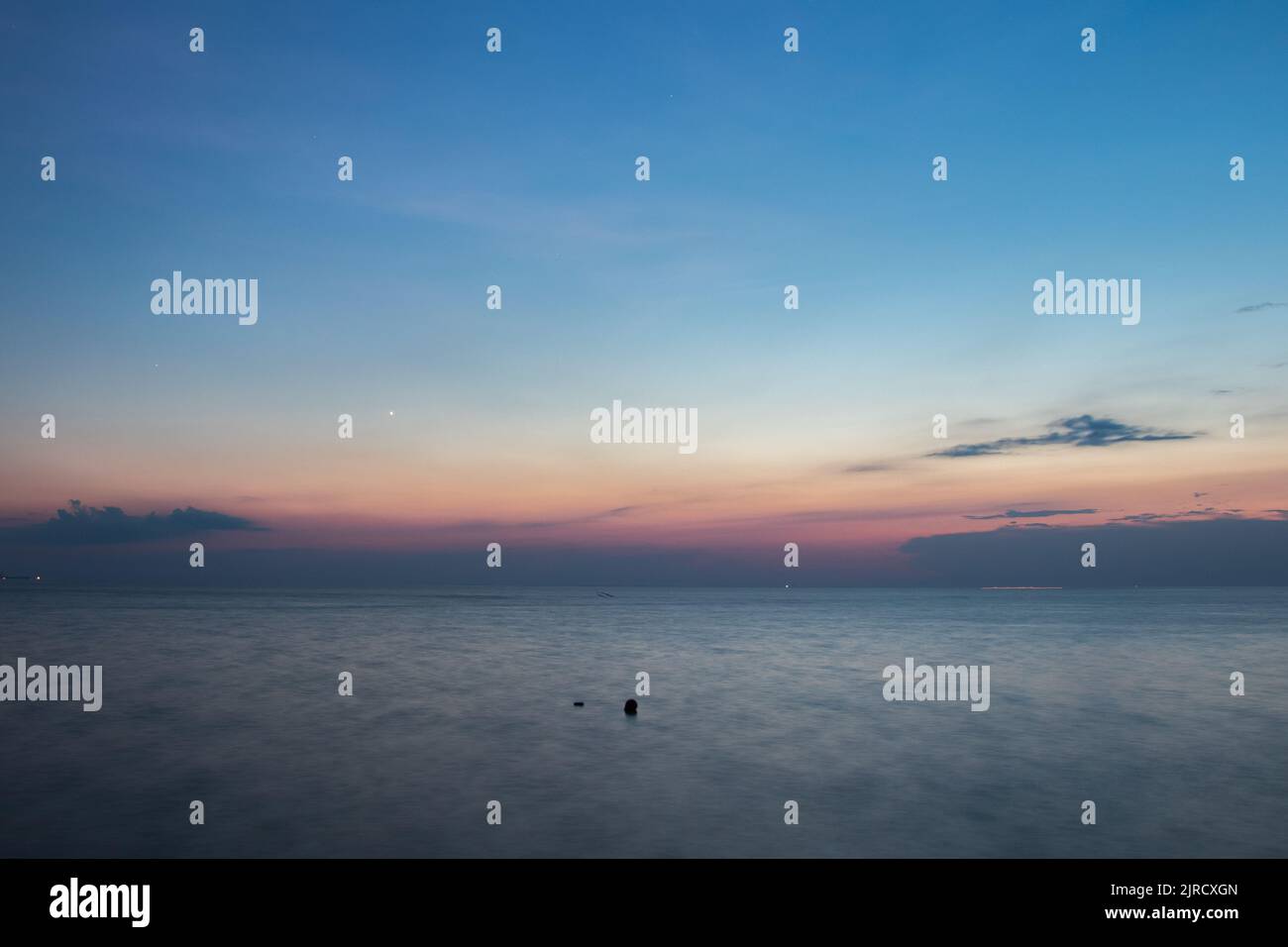A scenic shot of the calm ocean with the evening sunset on the horizon ...