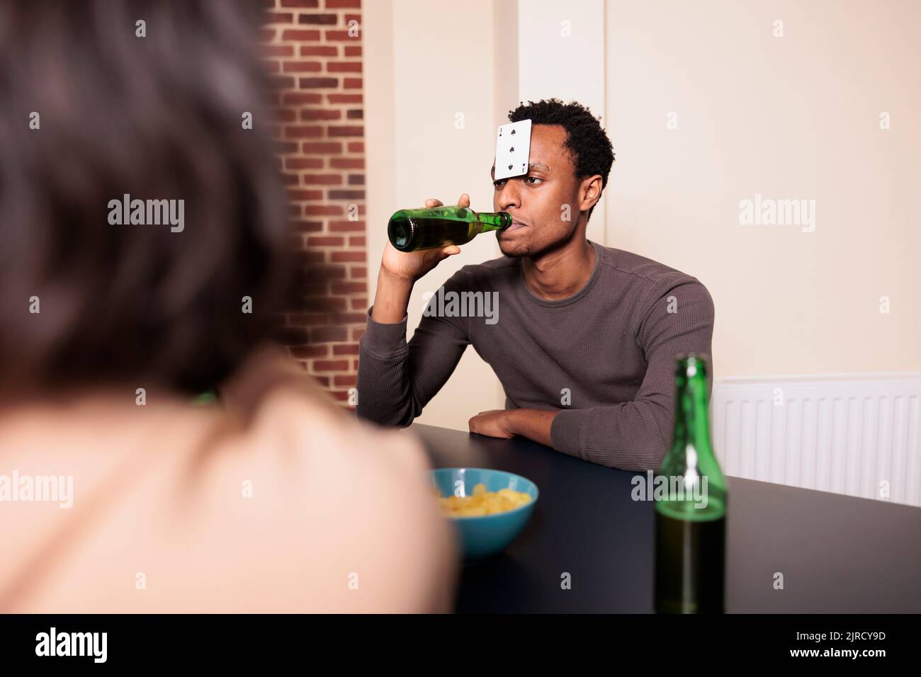 Confident young adult man with plastic card on forehead drinking beer ...