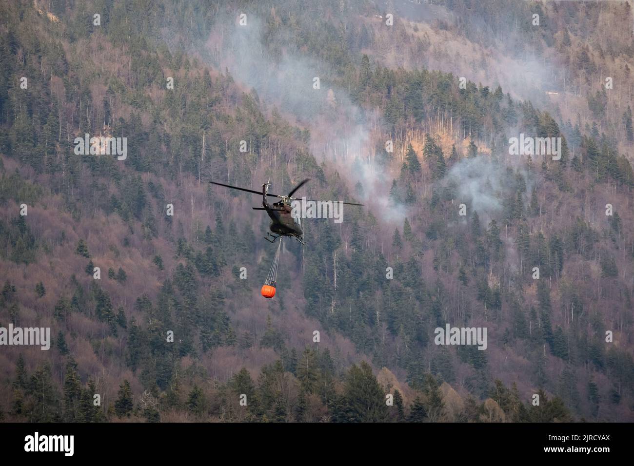Firefighting helicopter with a bucket suspended on a cable, collecting ...