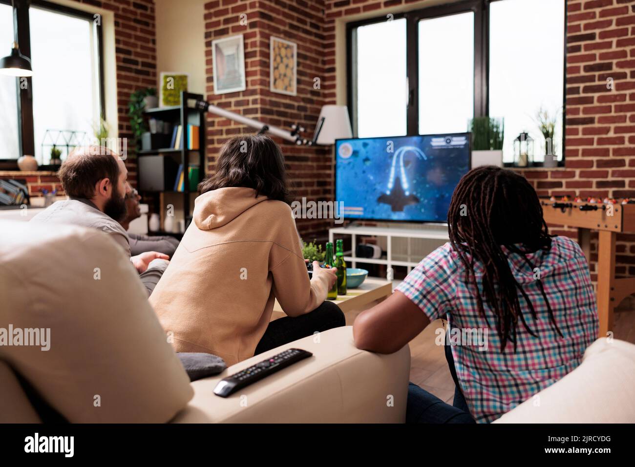 Multiethnic group of friends sitting on sofa at home while playing ...