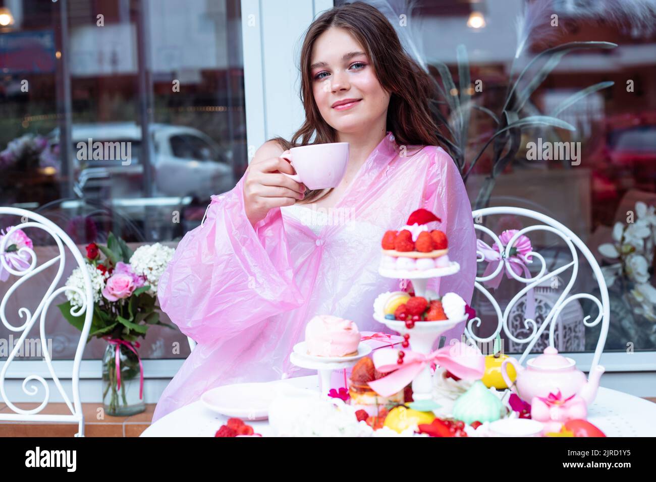 Pretty teenage girl in pink raincoat tasting sweet berry dessert cake ...