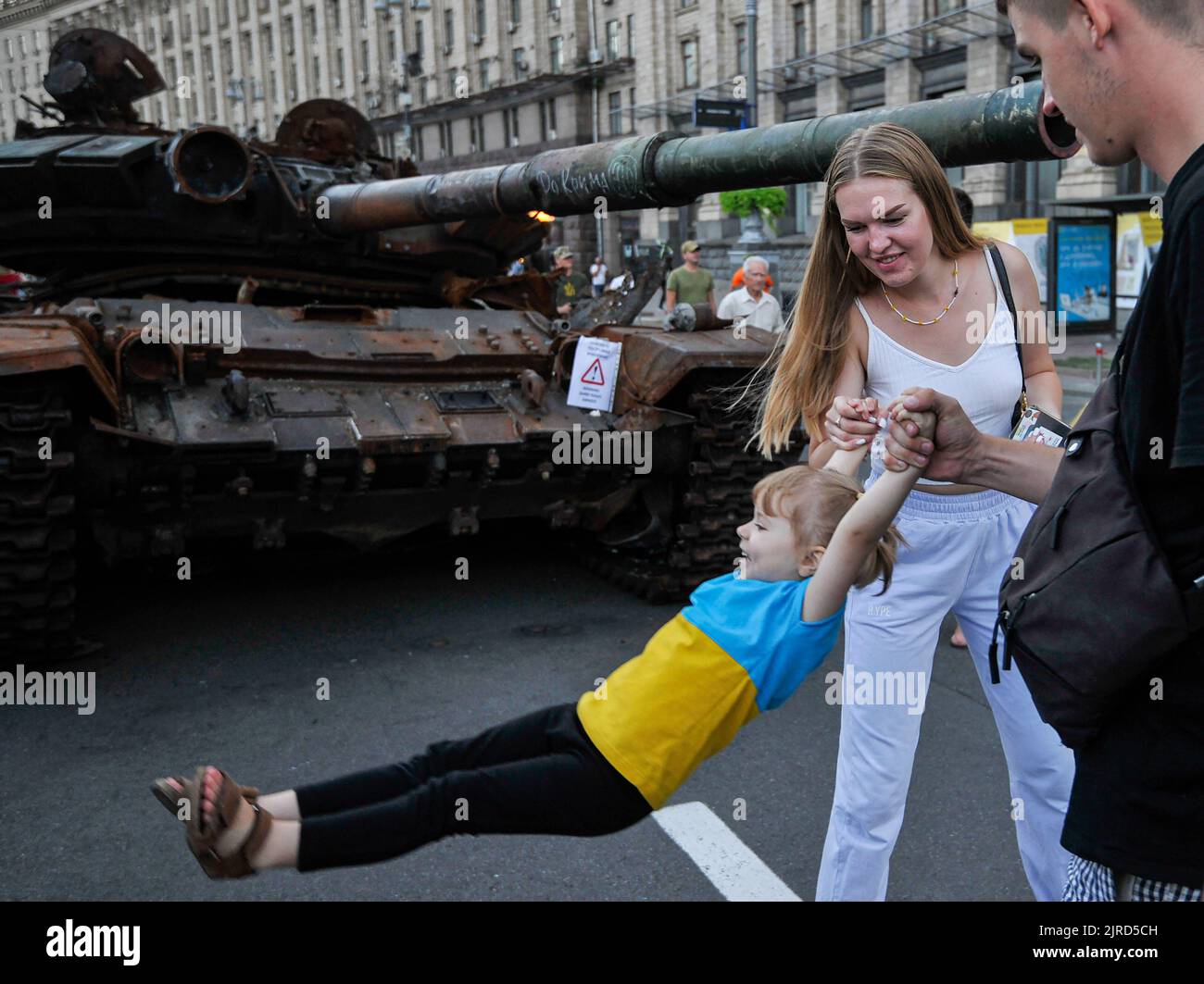 A man and woman hold a child next to destroyed Russian army equipment ...