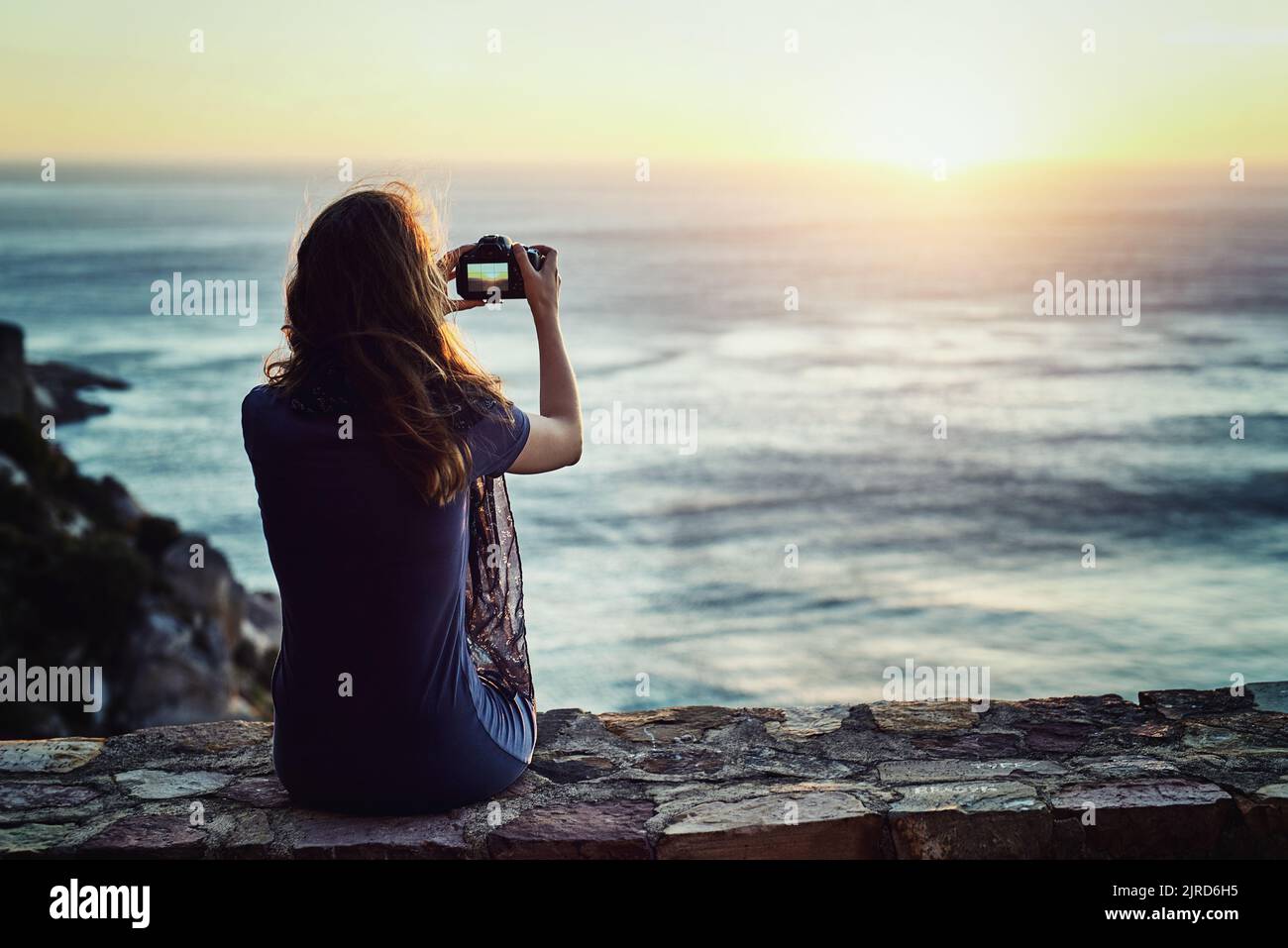 Capturing the beauty around her. Rearview shot of a young woman taking ...