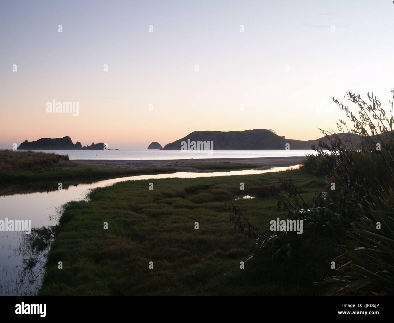 Sea and sunset sky beyond stream flowing across to sea at Opito Bay ...