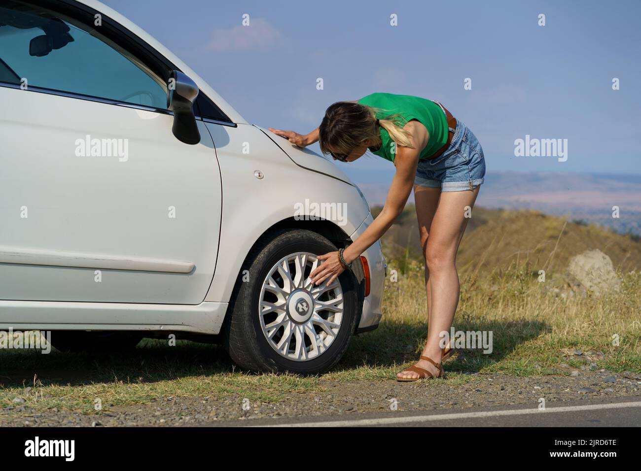 Woman leans down putting hand on wheel tire to check condition of white ...