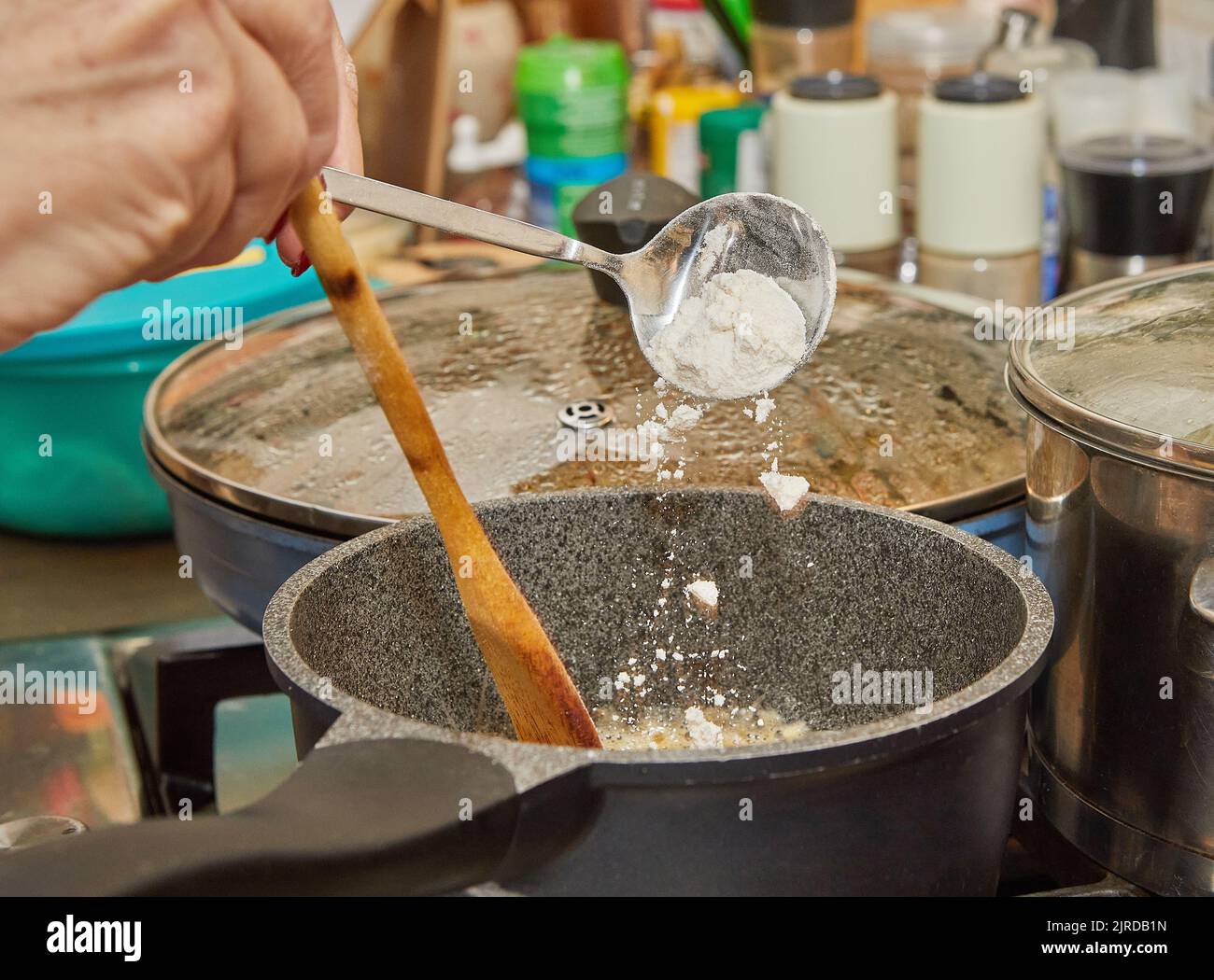Chef throws flour into pot of bechamel sauce being prepared on gas ...