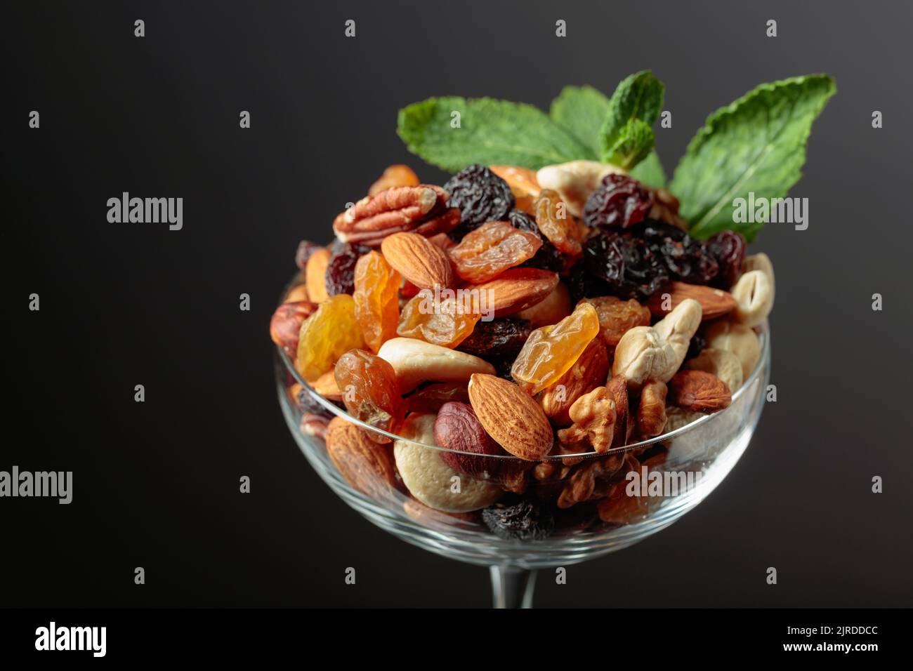 The mix of nuts and raisins in a glass bowl is garnished with mint on a ...